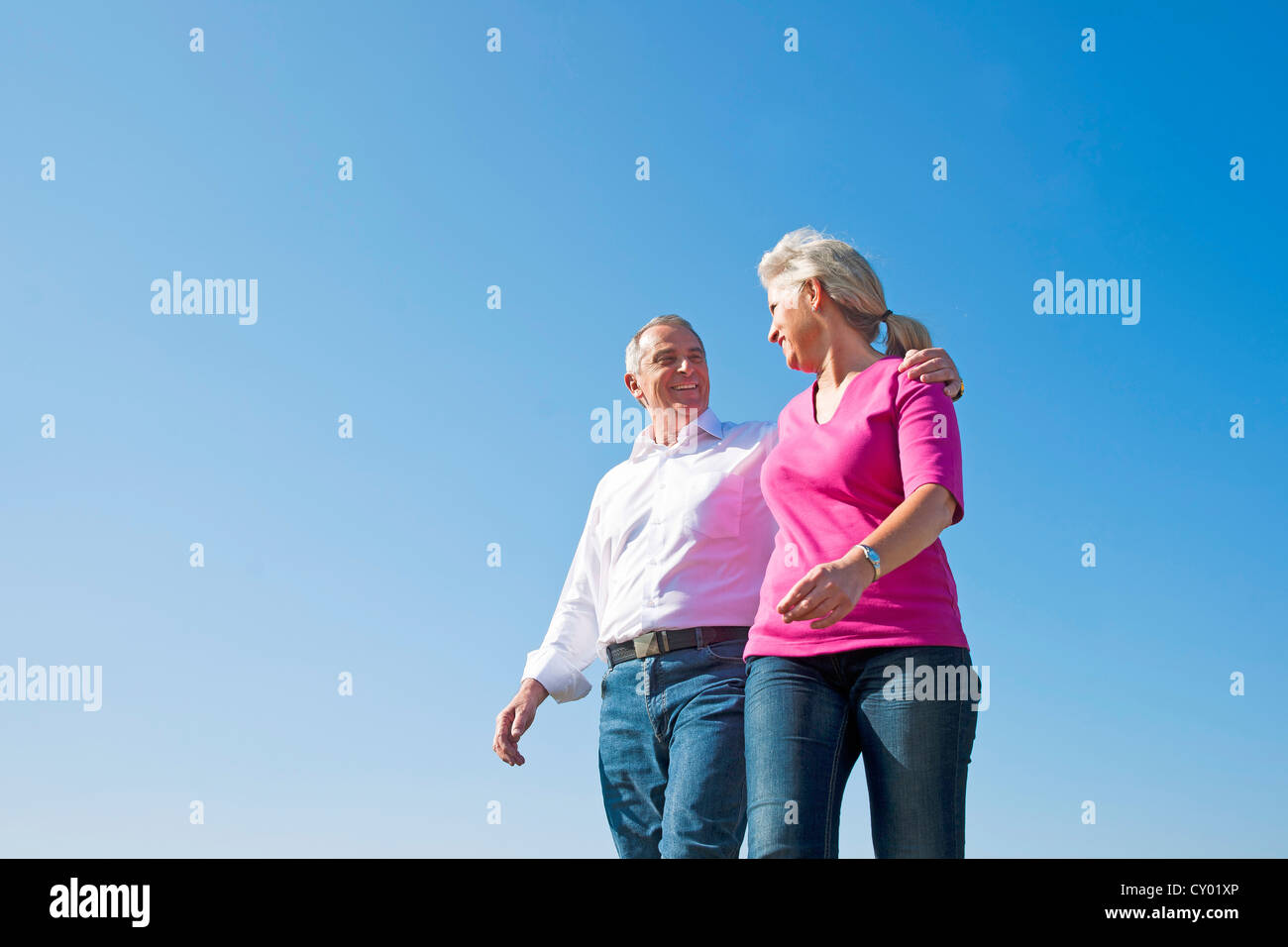 Middle-aged couple smiling as they walk in front of a blue sky Stock ...