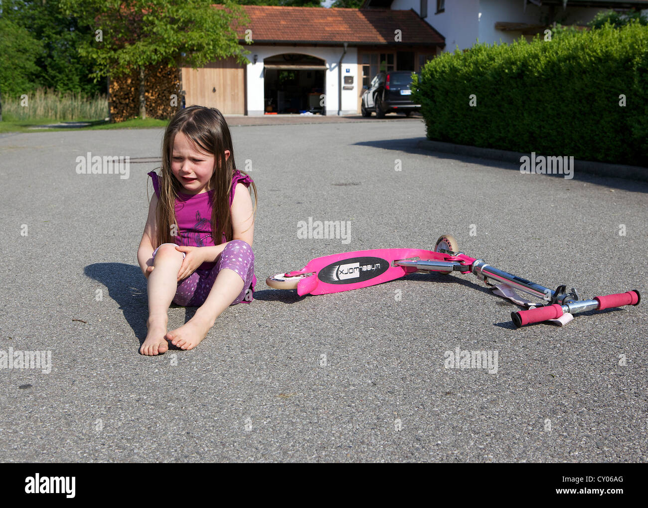 Little girl, three years, has fallen off her scooter, sitting on the ...