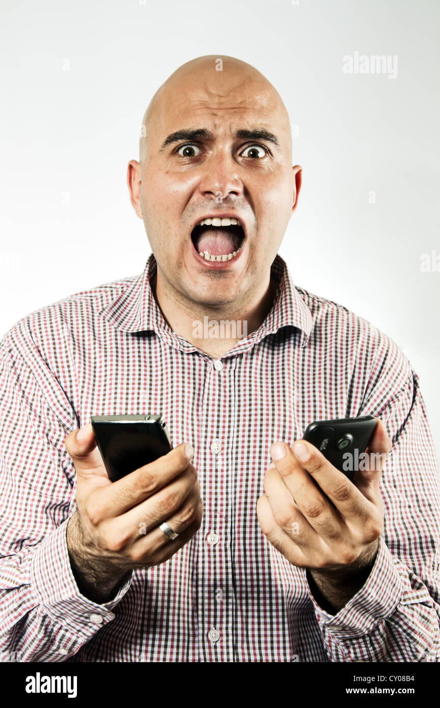 Stressed young adult businessman using two smartphone device at the ...