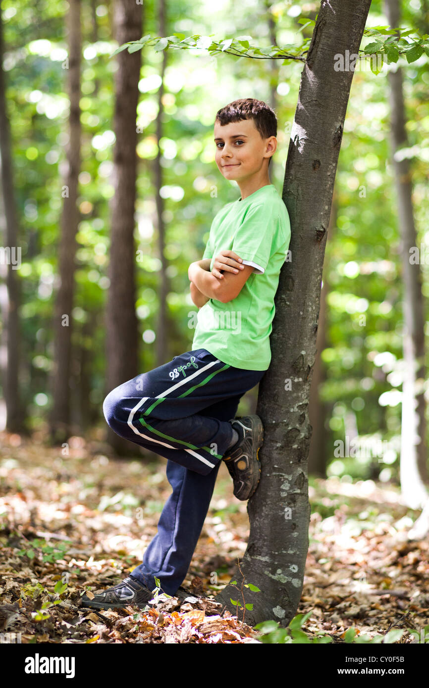 Full length portrait of a happy child leaning on a tree trunk with ...