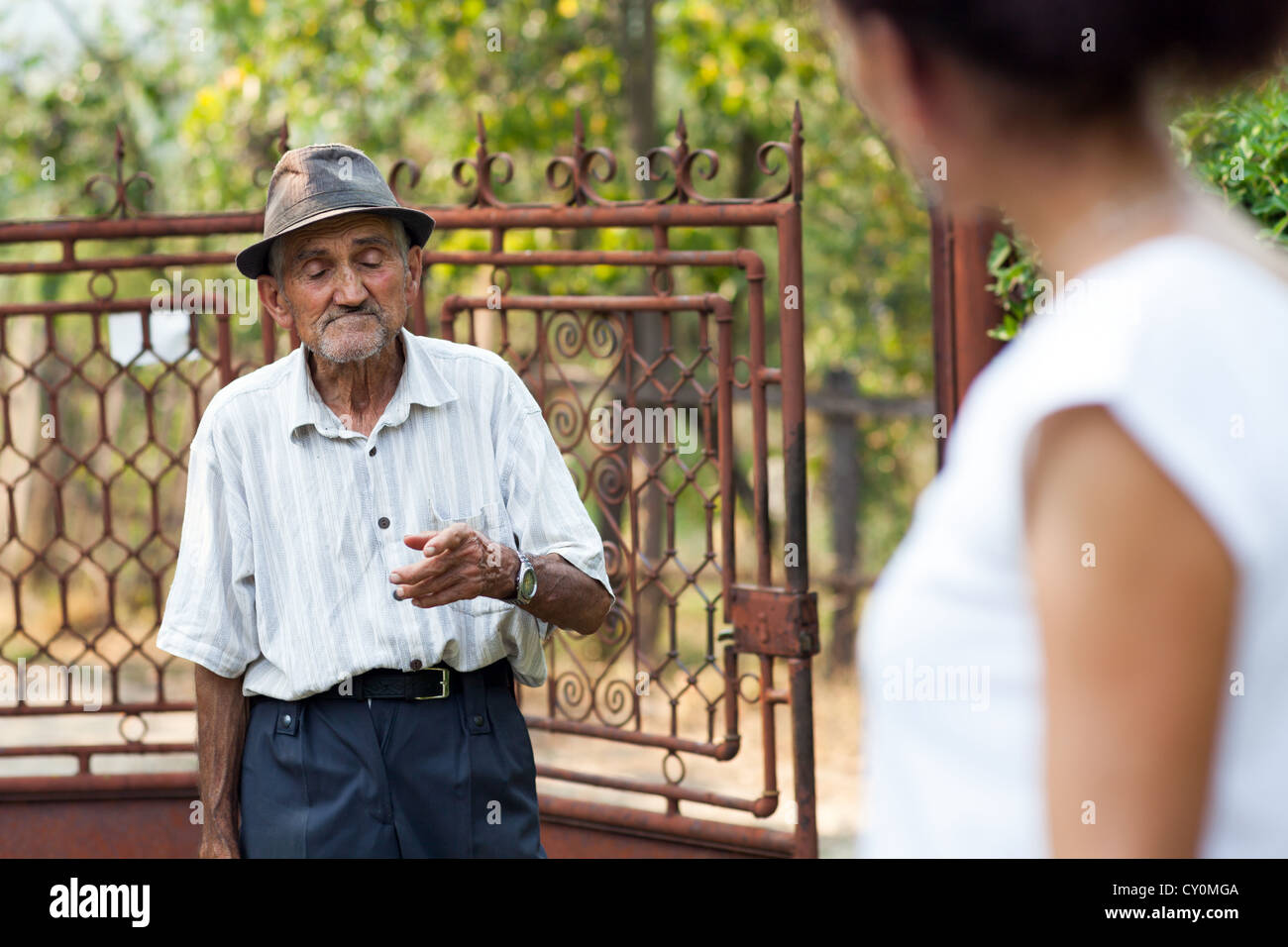 Portrait of an old man standing near a metal gate in the countryside ...