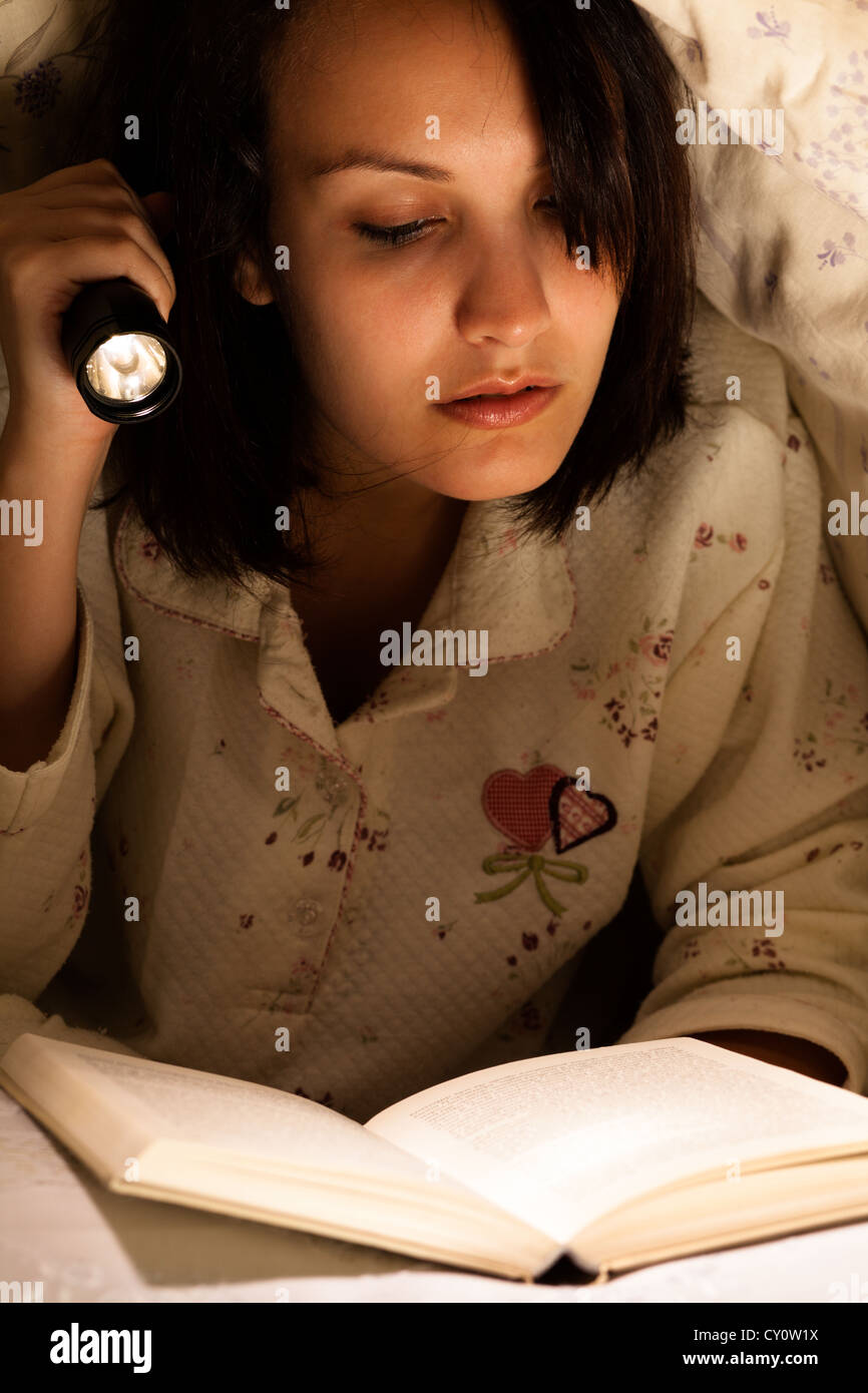 Serious Woman Reading a Book with Flashlight on Bed Stock Photo - Alamy