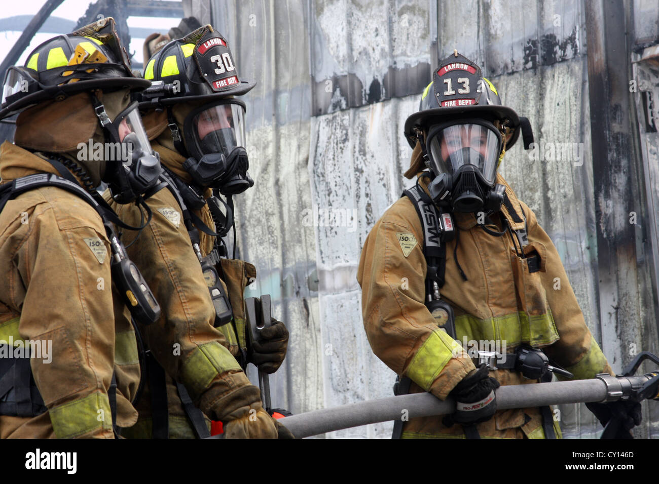 A woman firefighter holding a hose line and her male team members of ...