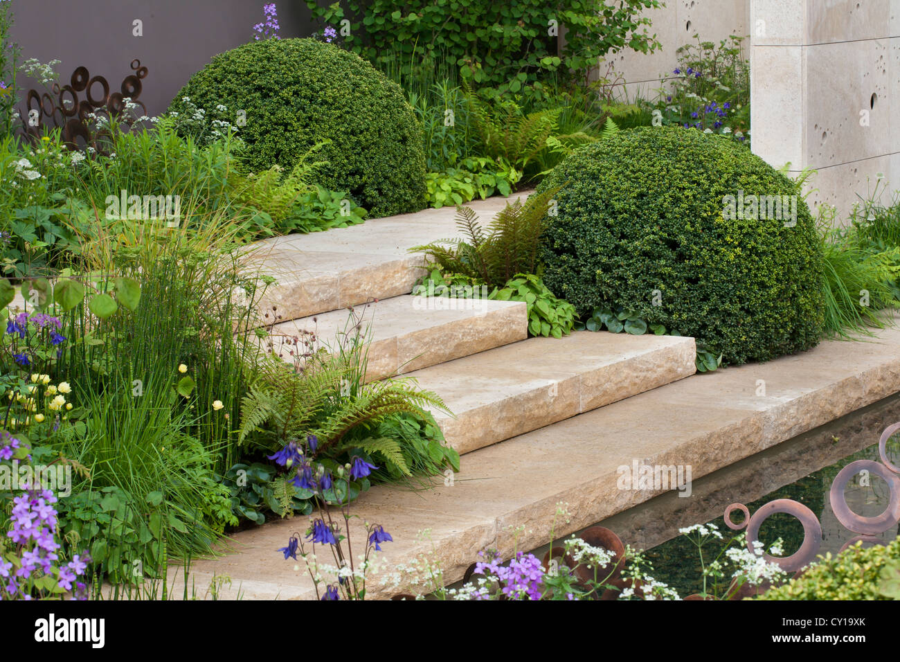 Contemporary designed garden with shaped shrubs and water feature. The ...