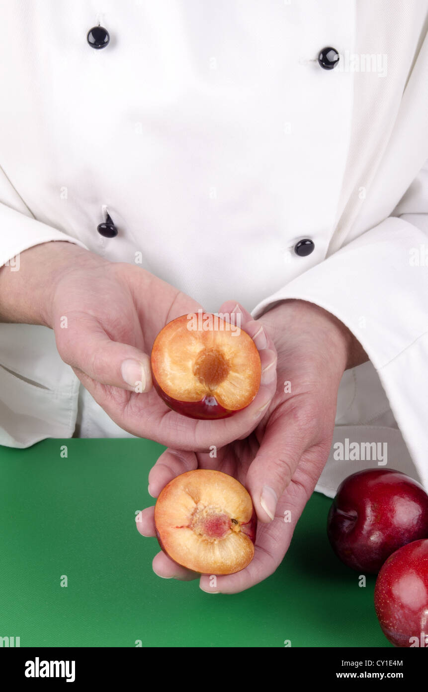 female chef in uniform female chef holds a cut through plum Stock Photo ...