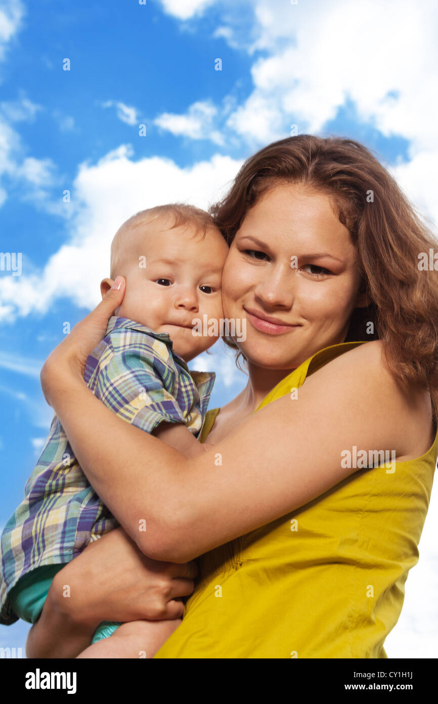 happy mom and son on cloudy background smiling and looking at camera ...