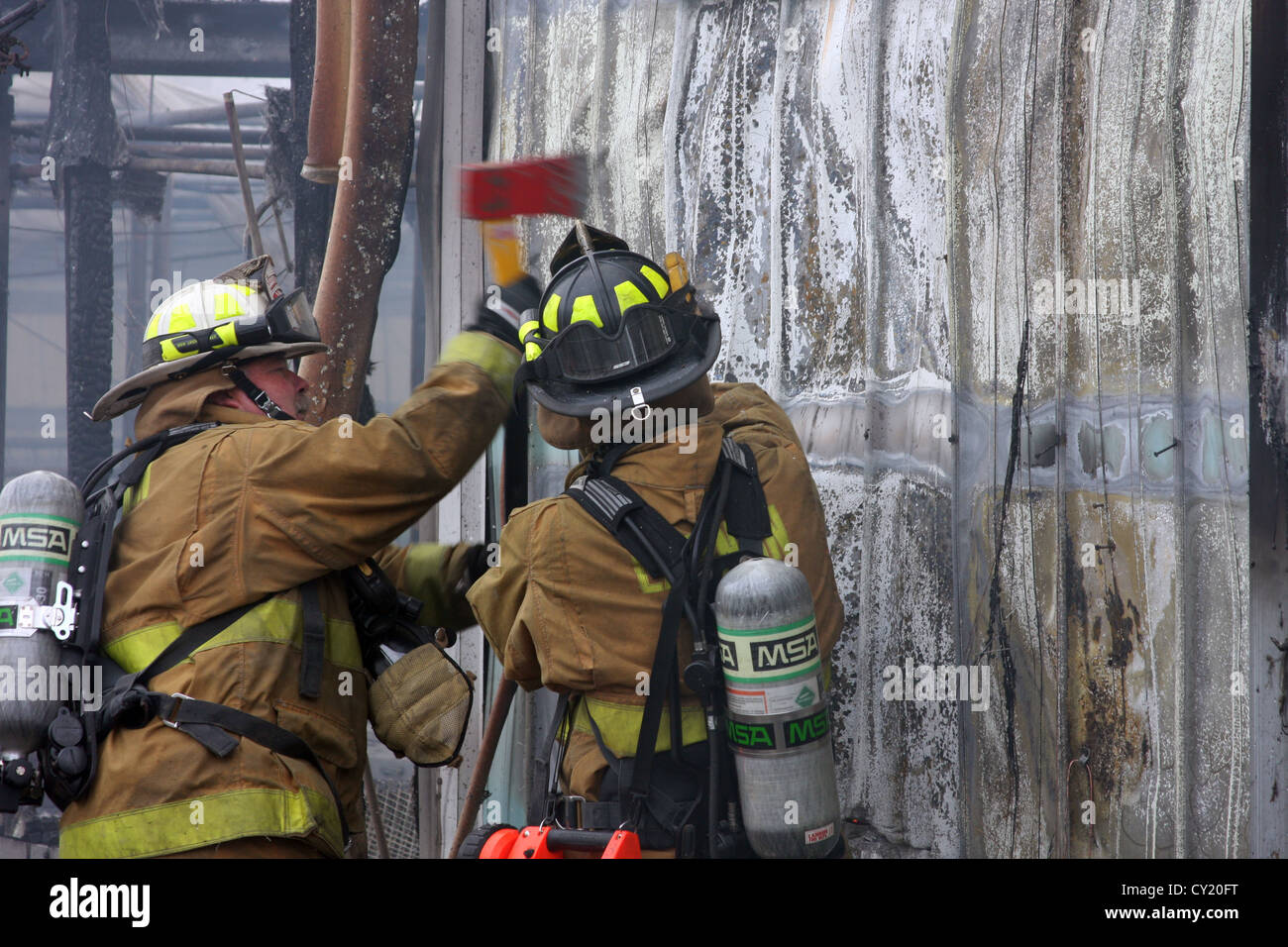 A firefighter using an ax to gain access to a burning area under a ...