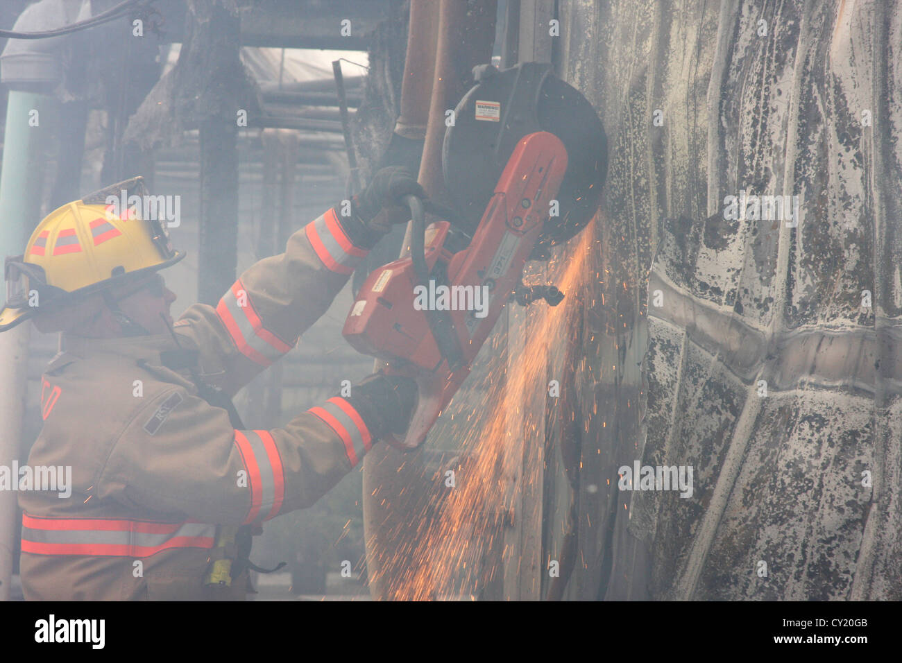 A firefighter using a saw to cut through a wall to gain access to a ...