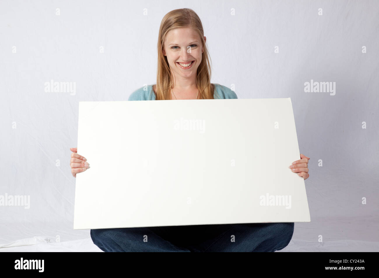 Pretty blond woman sitting and holding a white sign that is blank ...