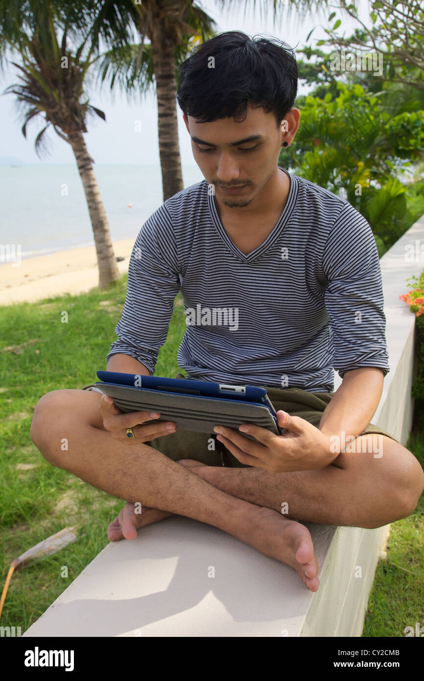 A young Thai guy using an Ipad by the beach, Chalong bay, Phuket Stock ...