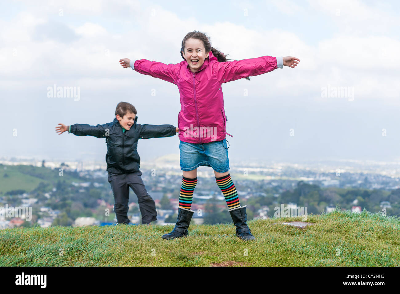 Two children, arms outstretched standing against strong winds on top of ...