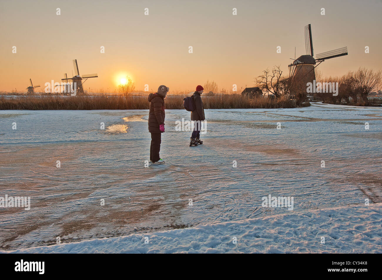 People skating on a frozen canal at sunset pass the Kinderdijk windmills near Rotterdam in the ...