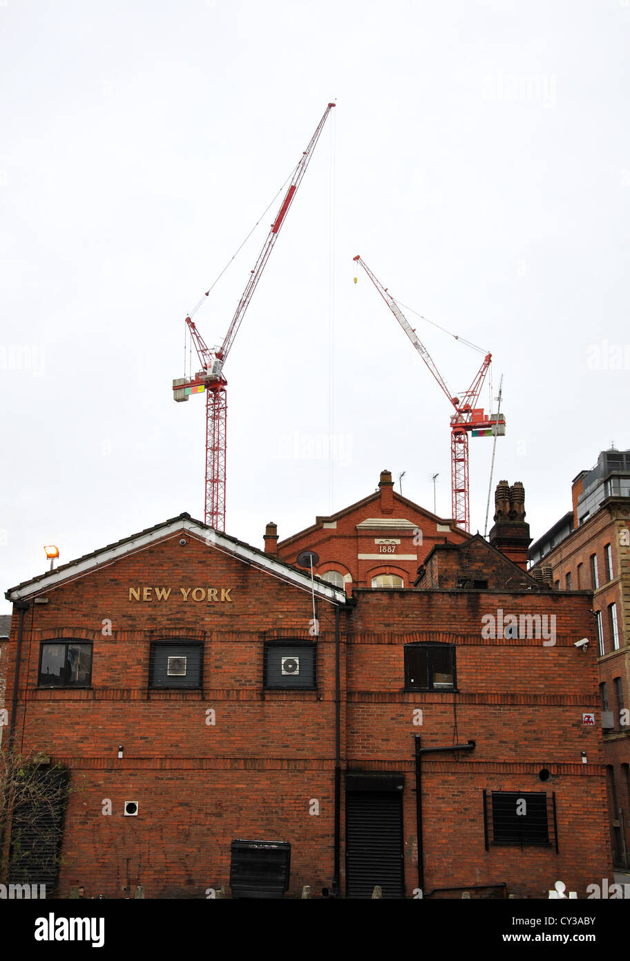 Facade of a small old factory in Manchester with cranes behind. UK ...