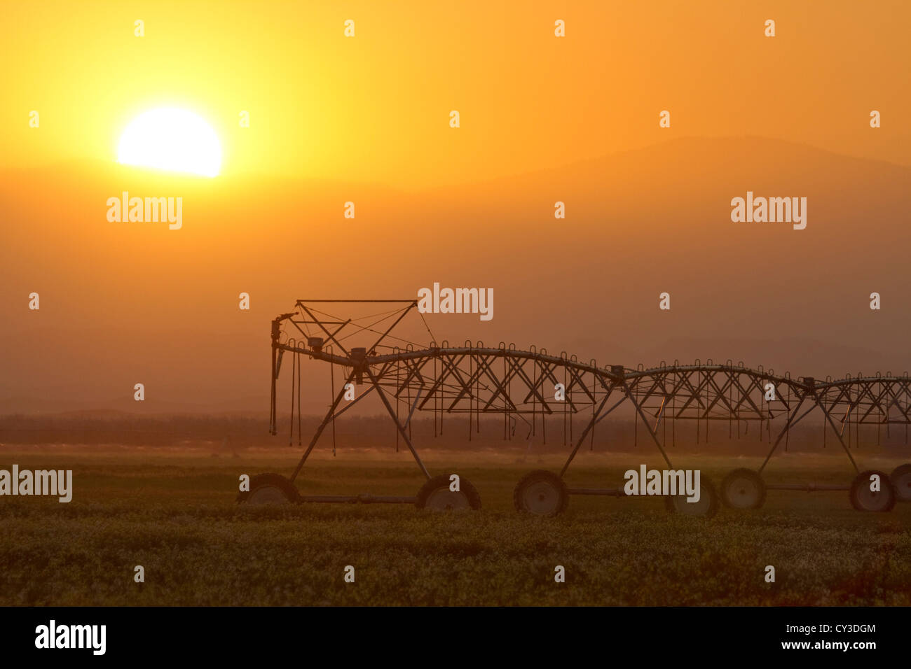 The sun sets behind a pivot irrigation boom in farmland in the ...