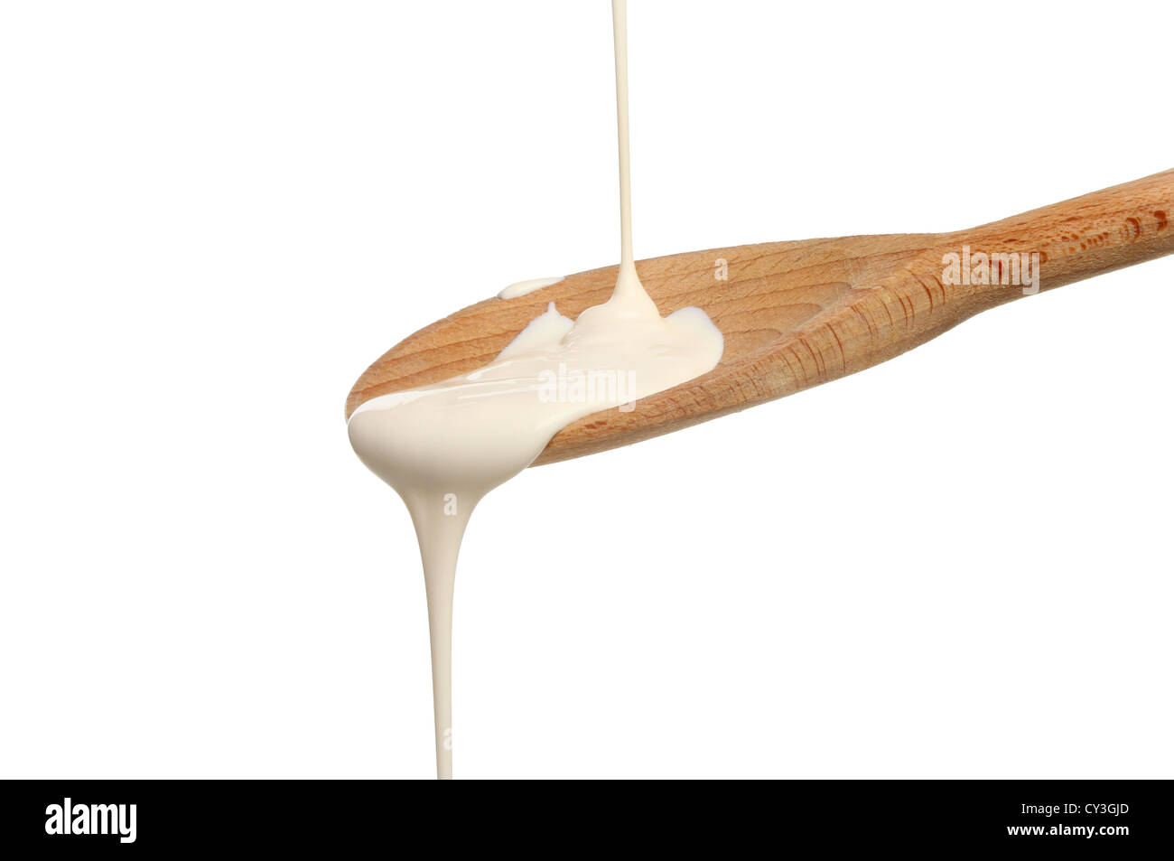 Cream pouring onto a wooden spoon isolated against white Stock Photo ...