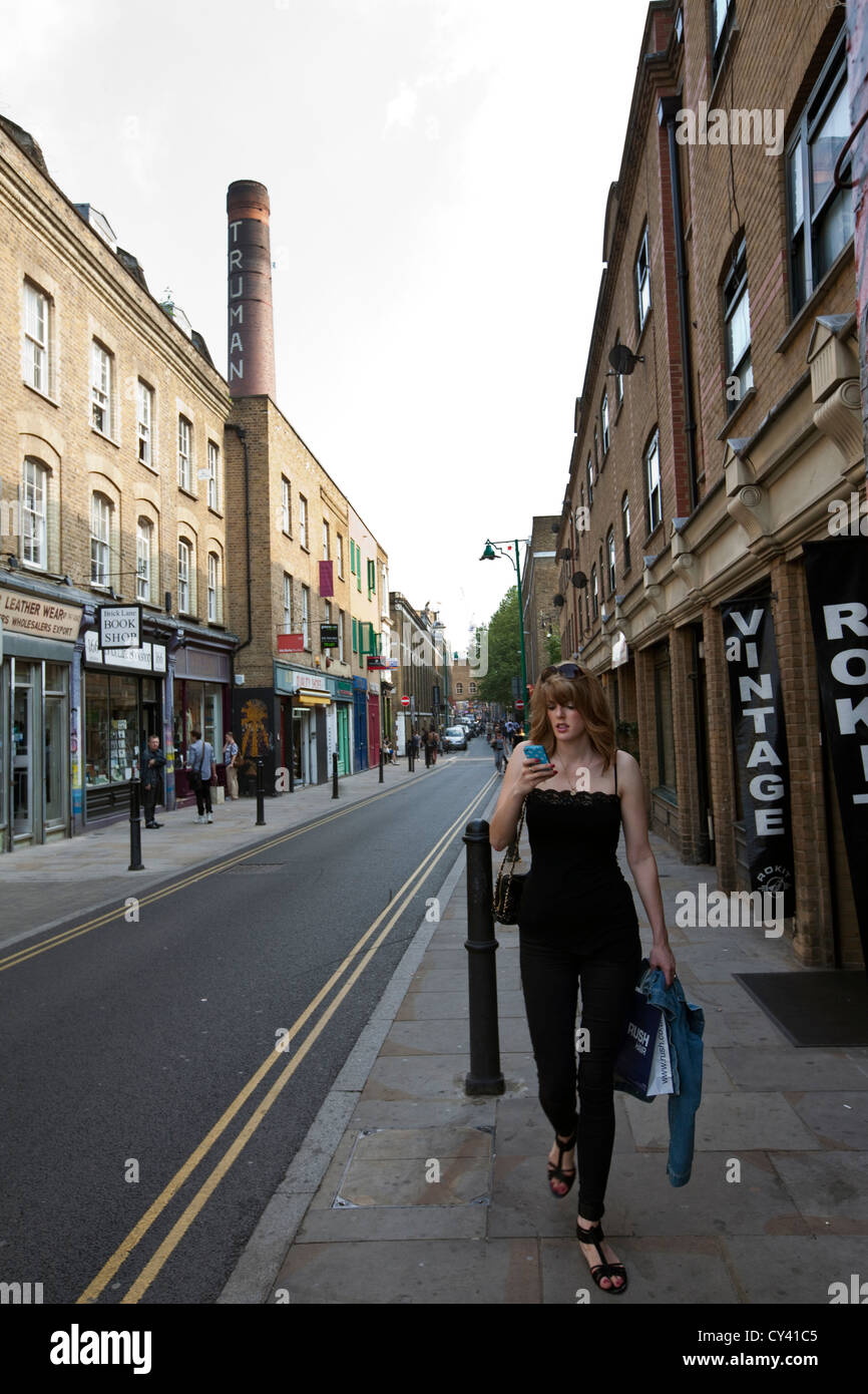 A woman checks her mobile telephone device as she walks down Brick Lane ...