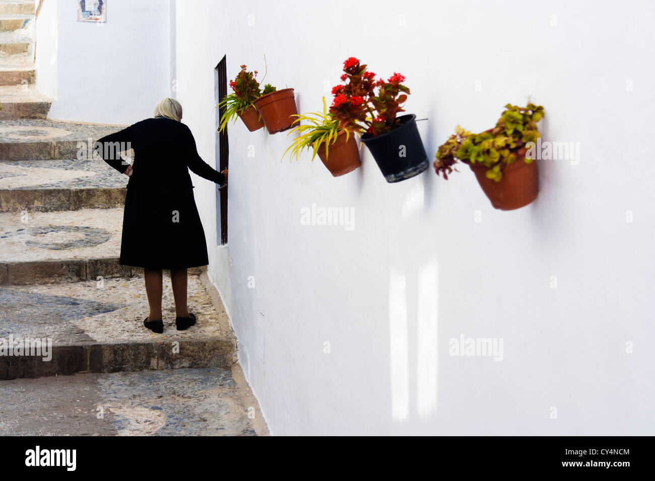 Old Spanish widow dressed in black on her way up the cobbled paved ...