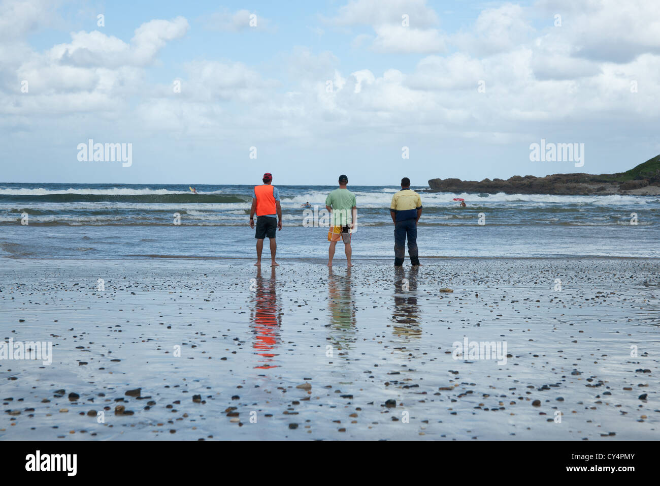 Three men at waters edge watching nippers surf lifesavers training at ...