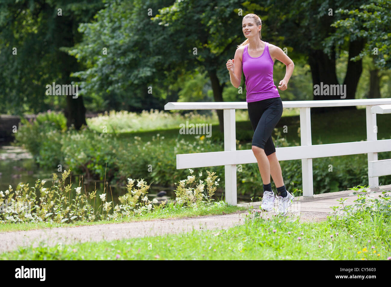 Young woman running over bridge in park Stock Photo - Alamy