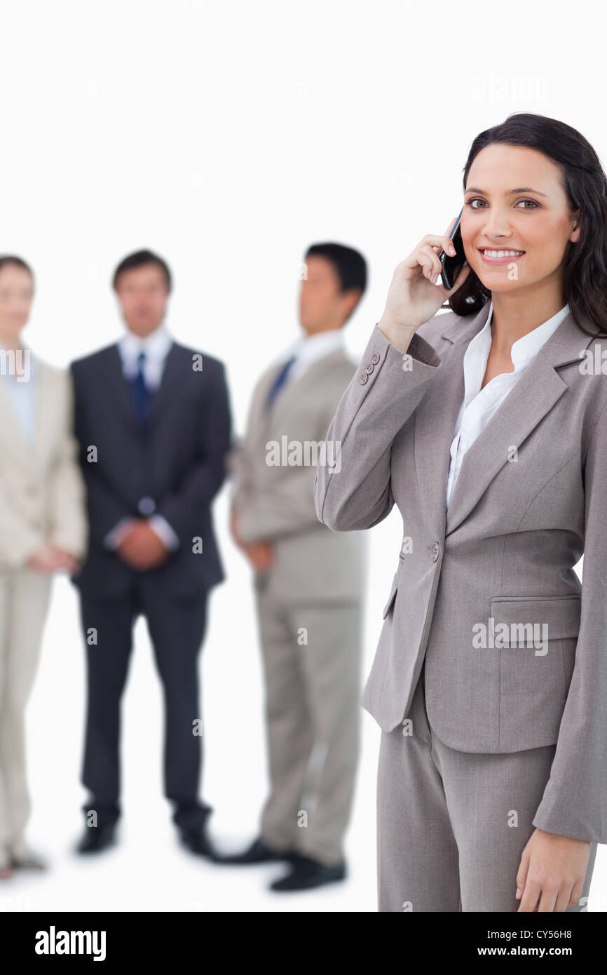 Smiling saleswoman on cellphone with team behind her Stock Photo - Alamy