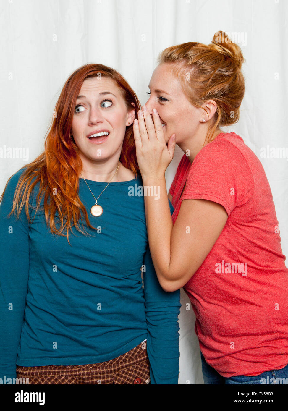 Studio Shot, Young women whispering in friend's ear Stock Photo - Alamy