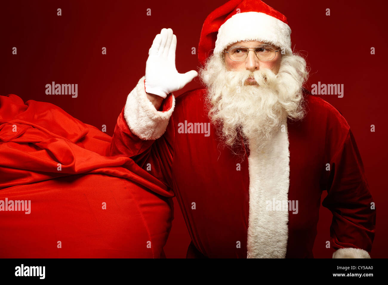 Portrait of Santa Claus raising his hand with huge red sack near by ...