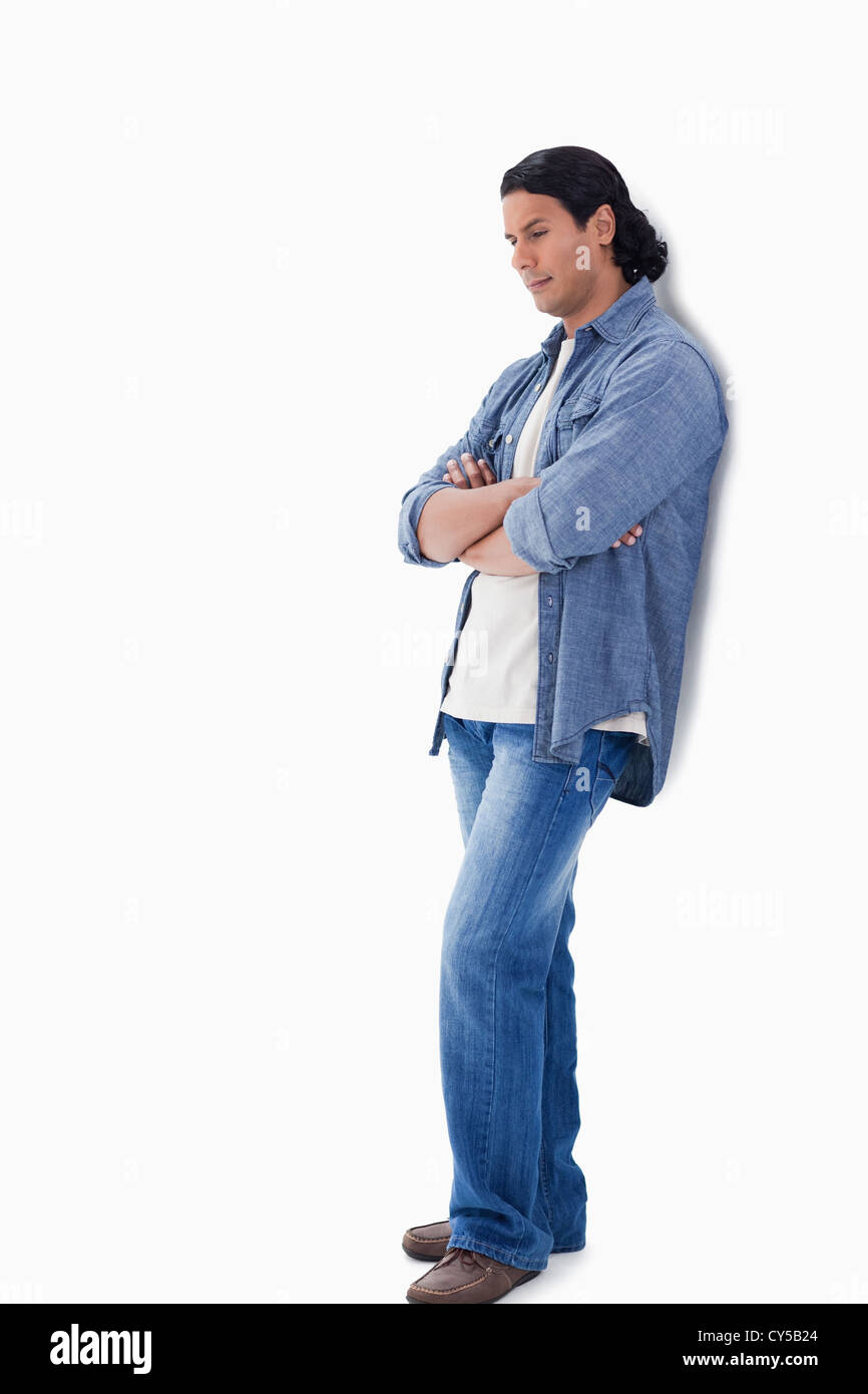 Man crossing his arms looking down and leaning against a wall Stock ...