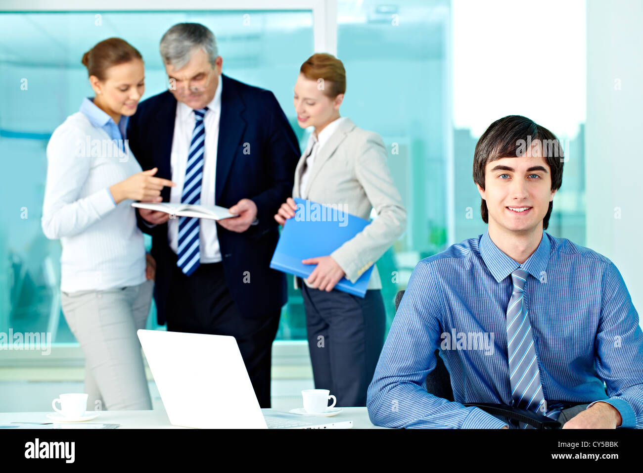 Portrait of confident leader looking at camera with working employees ...