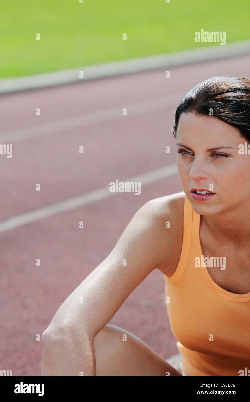 athletic young sportswoman, sitting alone on cinder track in stadium ...