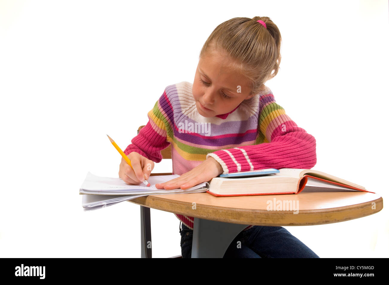 young girl concentrating on work at school desk, correcting a mistake ...
