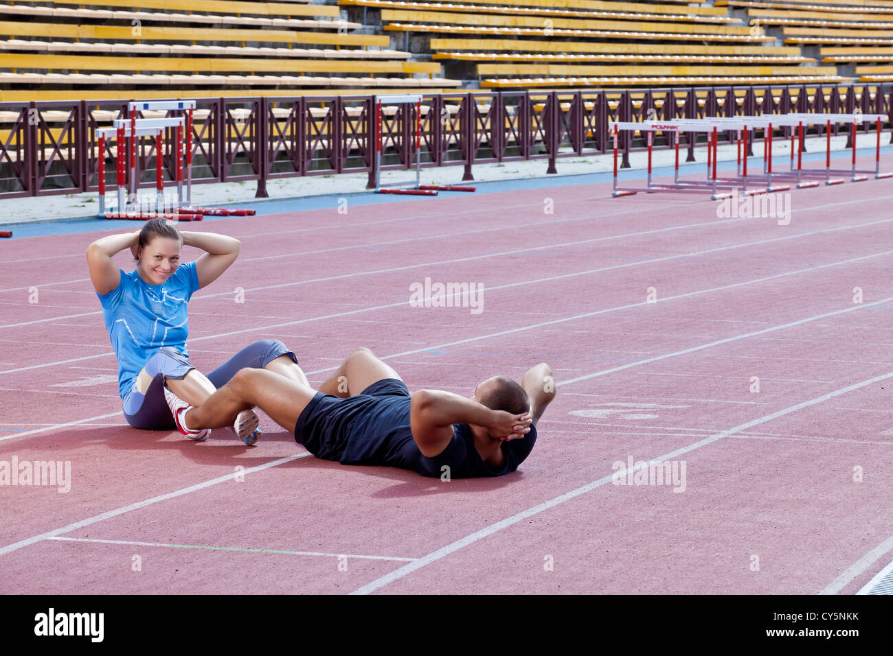 Two athletes help each other to pump the abdominals at the stadium on a ...