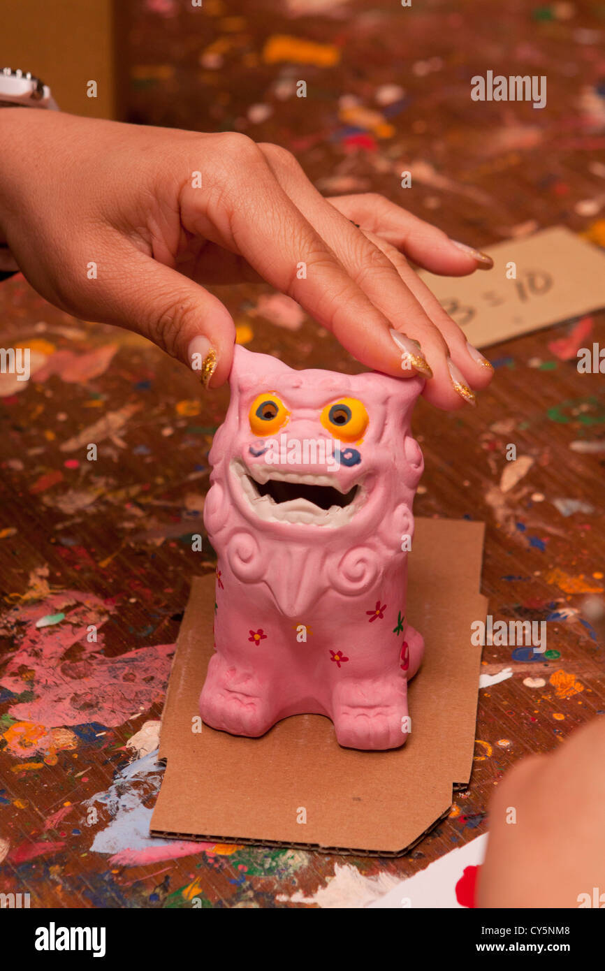 A young woman paints a pottery Shiisa - the stone lion god of Okinawa ...