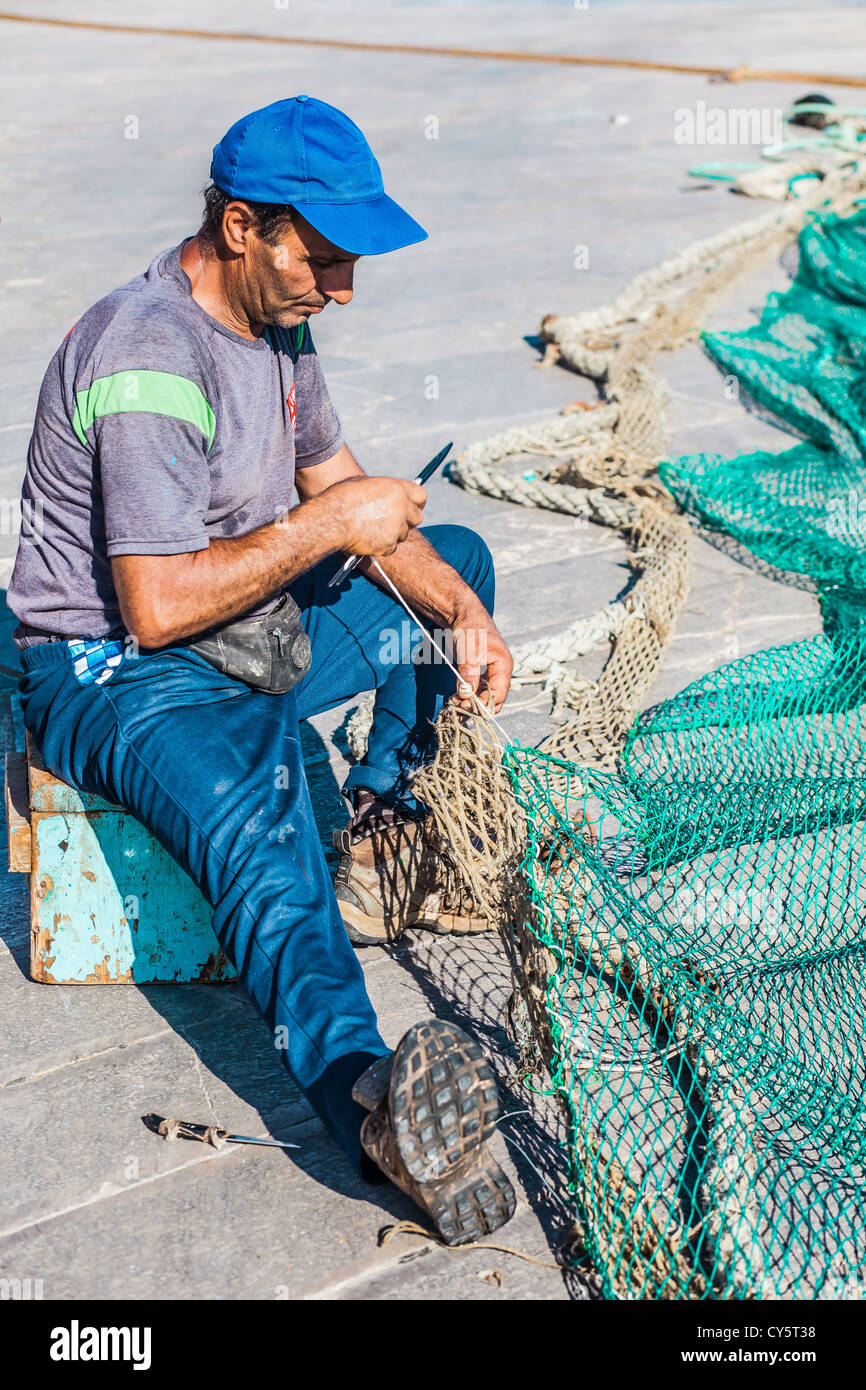 Fisherman on the harbor, fixing his fishing net Stock Photo - Alamy
