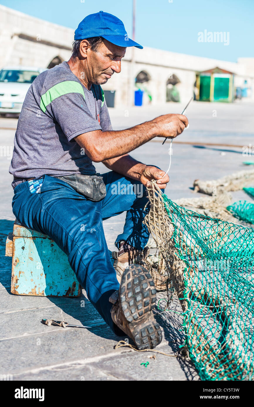 Fisherman on the harbor, fixing his fishing net Stock Photo - Alamy