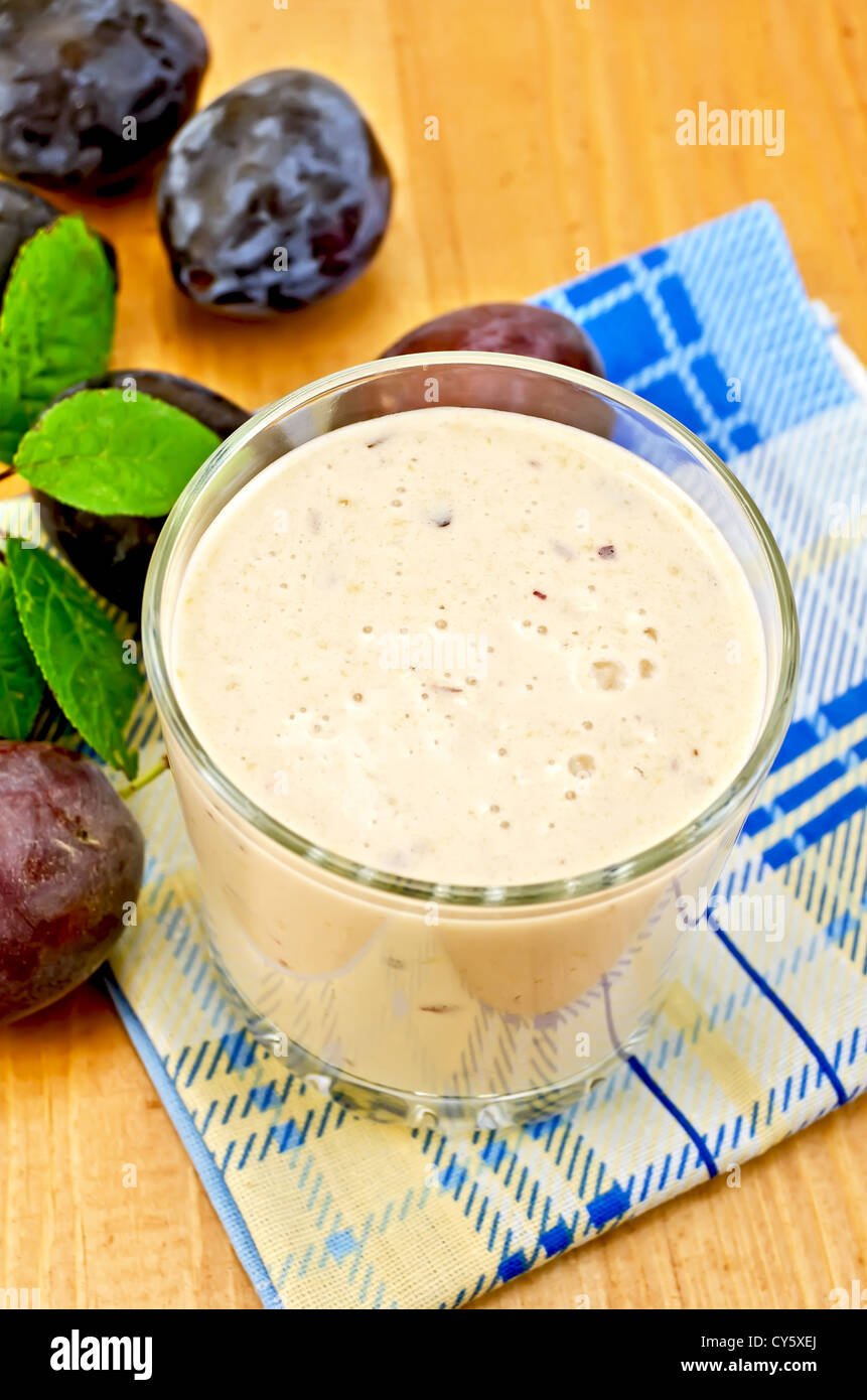 Milk shake in a glass beaker with plums on a napkin on the background ...