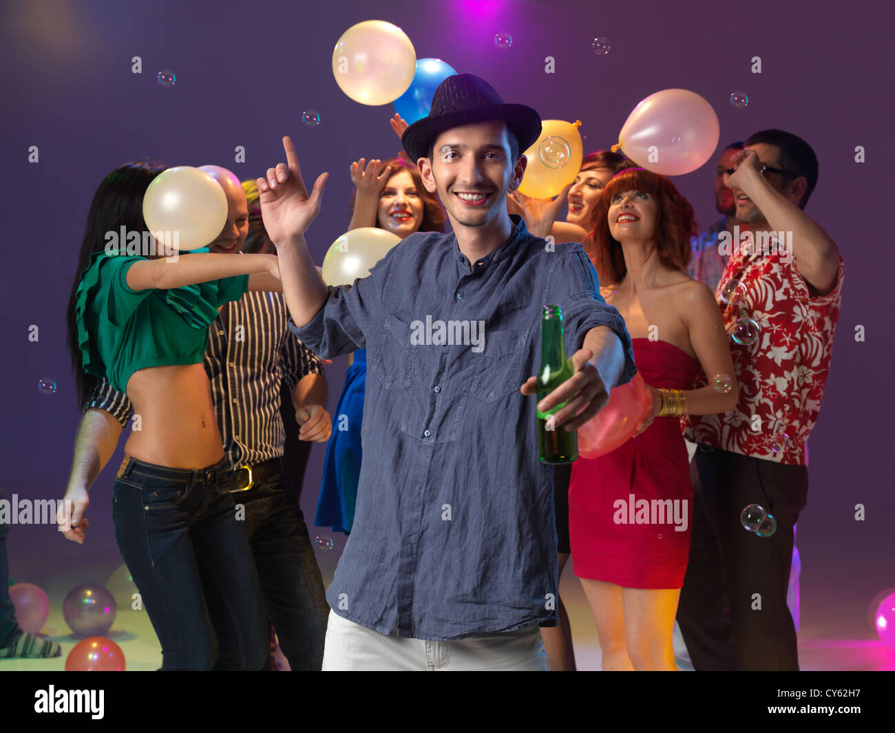 young man enjoying himself at party, holding a drink, with friends ...