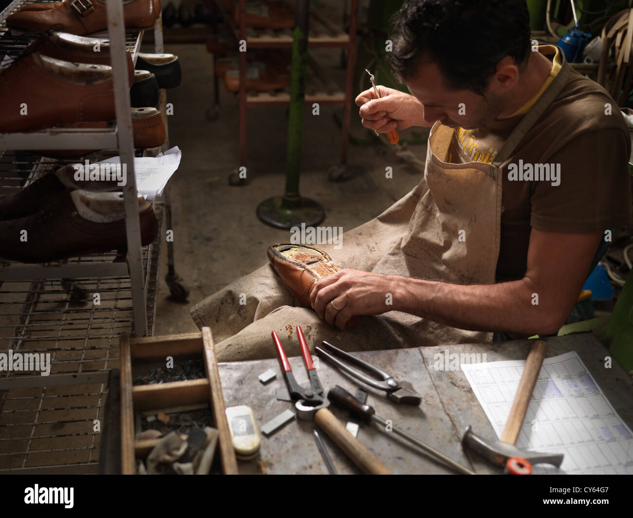 adult man working in a shoe factory, sewing the soles of the shoes ...