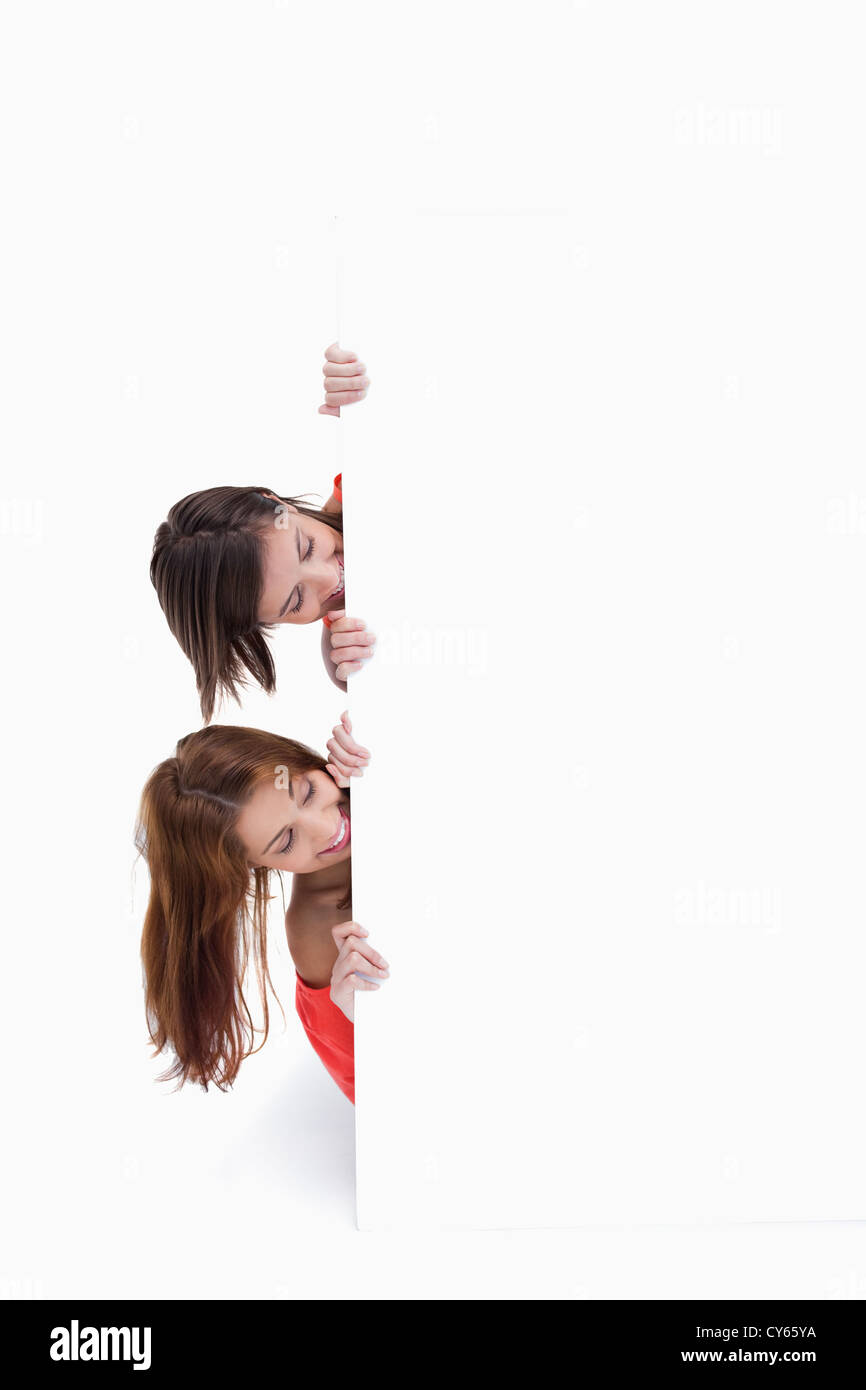Teenagers hiding behind a blank poster while showing their heads on the ...