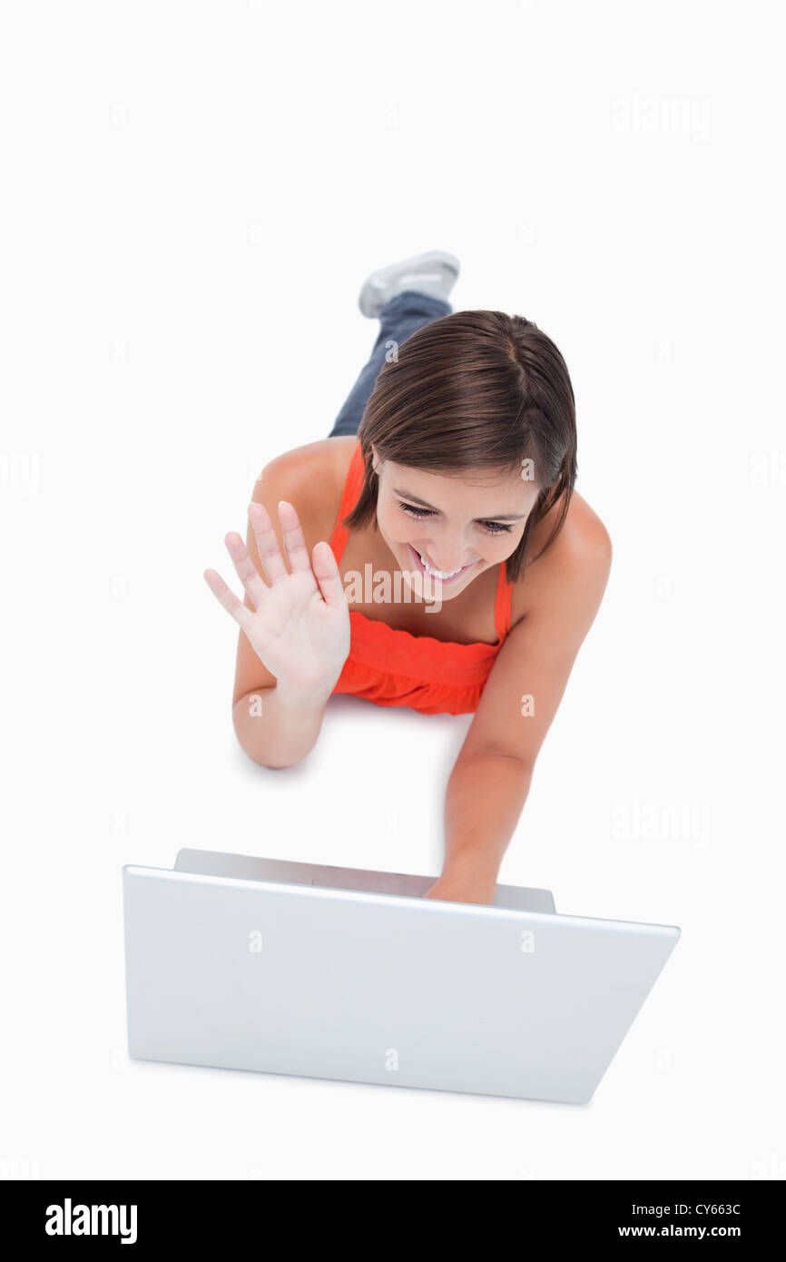 Attractive young woman saying hello to her computer while lying down ...