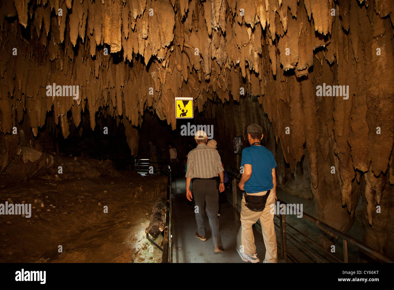 People walk under a sign warning to be careful of low stalactites in ...
