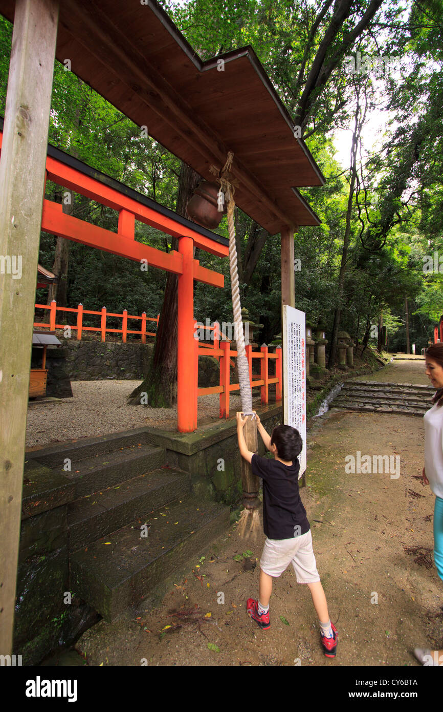 A young boy rings a large bell at the entrance to a small Shinto shrine ...