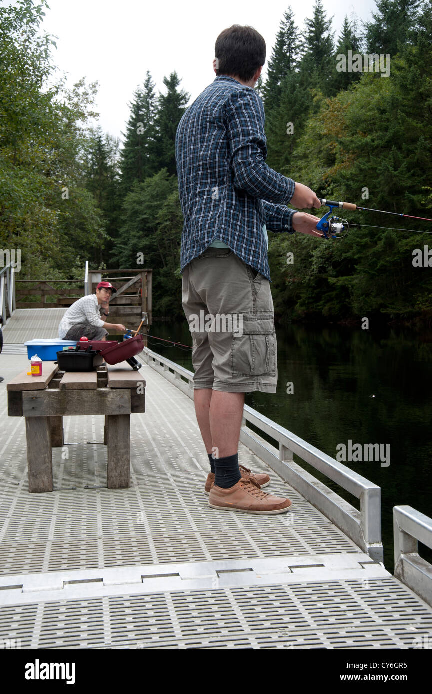 Two friends fishing off of a dock, fishing rods in the water Stock ...