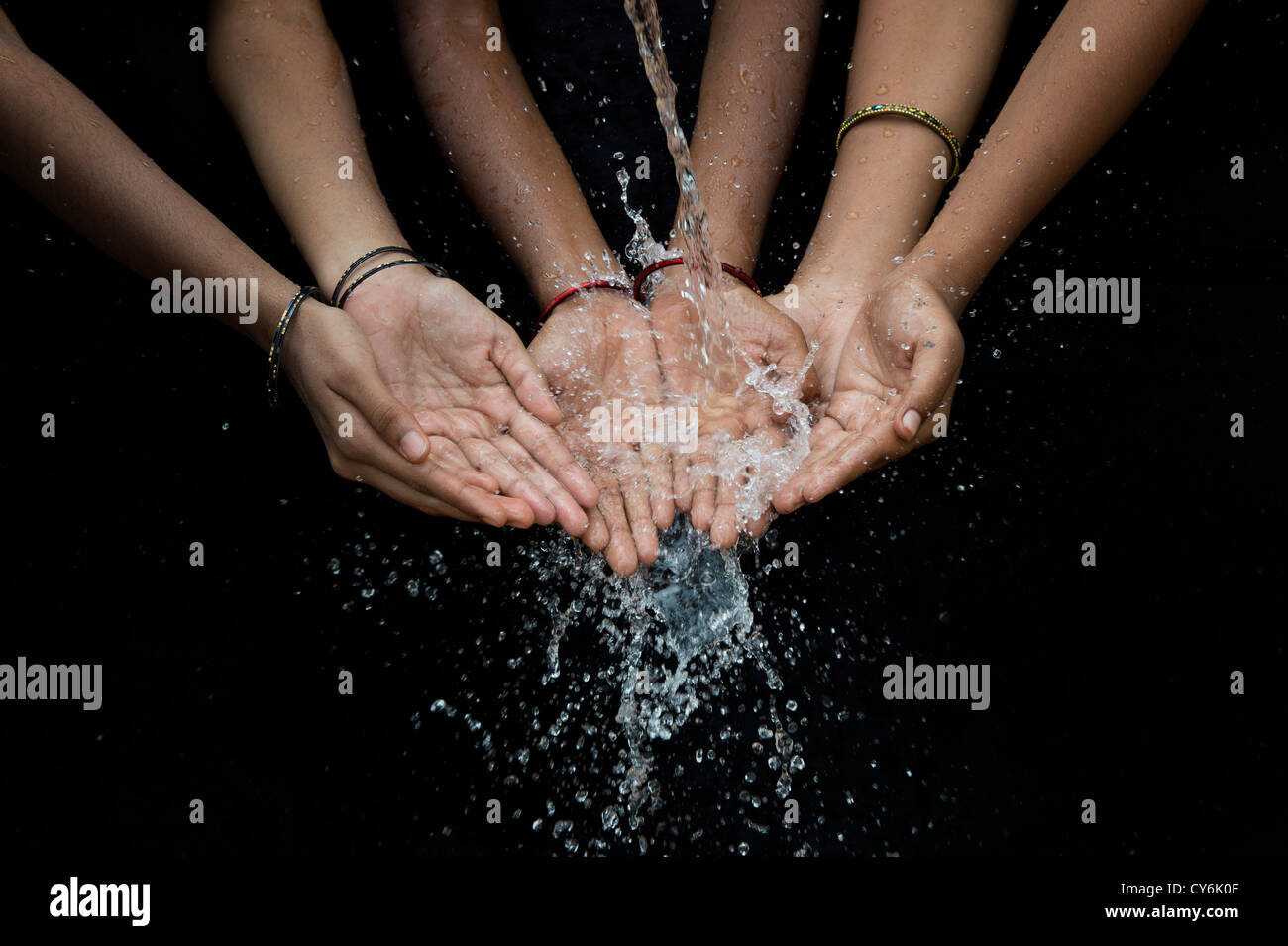 Three Indian girls cupped hands catching poured water against black ...
