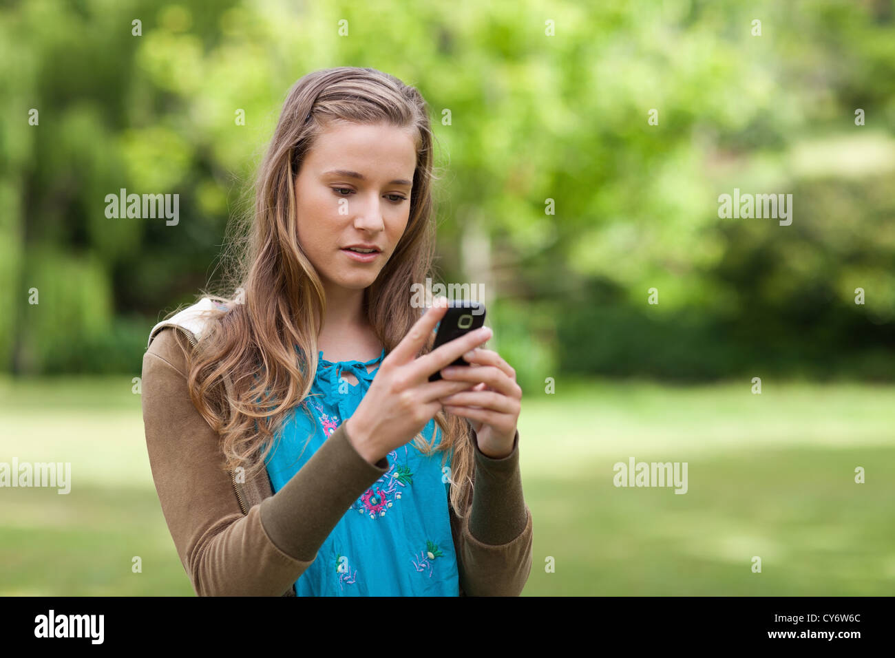 Serious teenage girl sending a text while standing in a park Stock ...