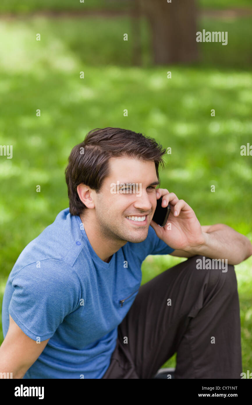 Young smiling man calling with his cellphone while sitting in a park ...