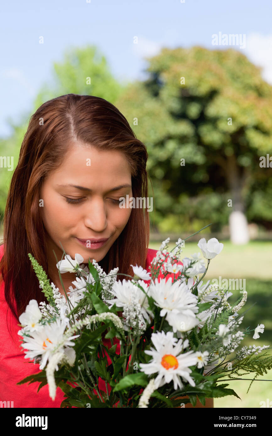 Young woman looking down at a flowers while standing in a park Stock ...