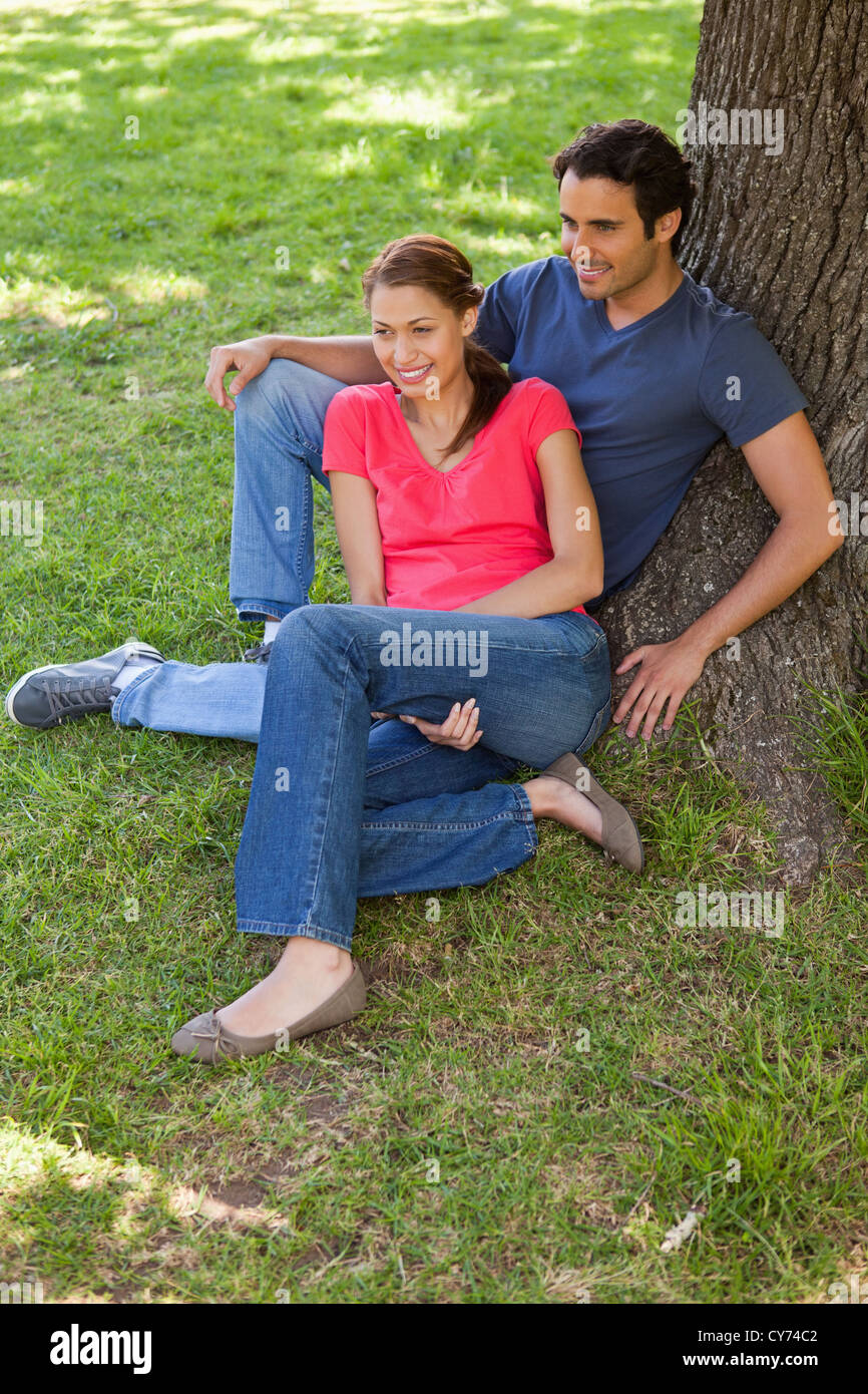 Two friends sitting together against a tree Stock Photo - Alamy