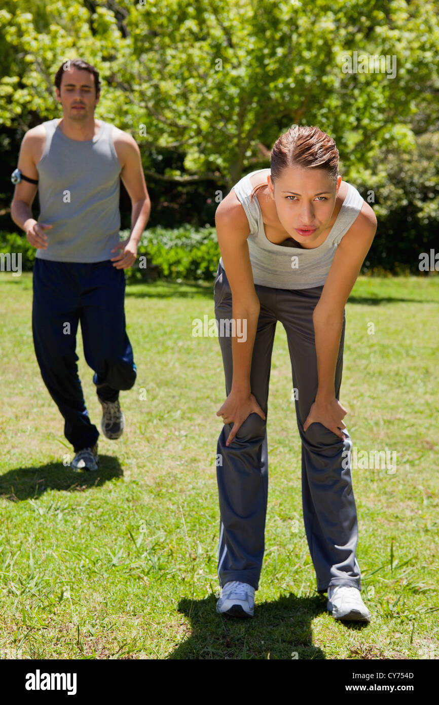 Woman bending over while a man is jogging in the background Stock Photo ...