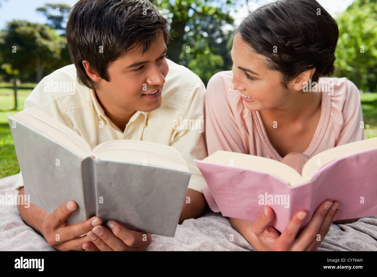 Two friends smiling at each other while reading on a blanket Stock ...