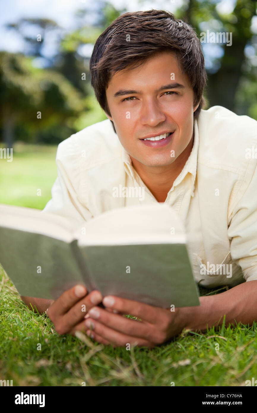 Man looking ahead while reading a book as he lies on grass Stock Photo ...